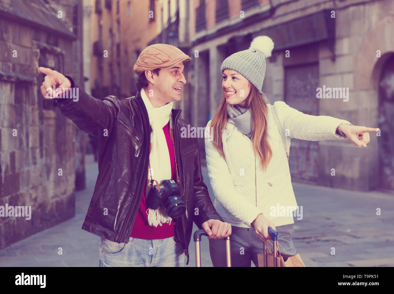Two smiling adult tourists in hats and scarfs pointing finger on ...