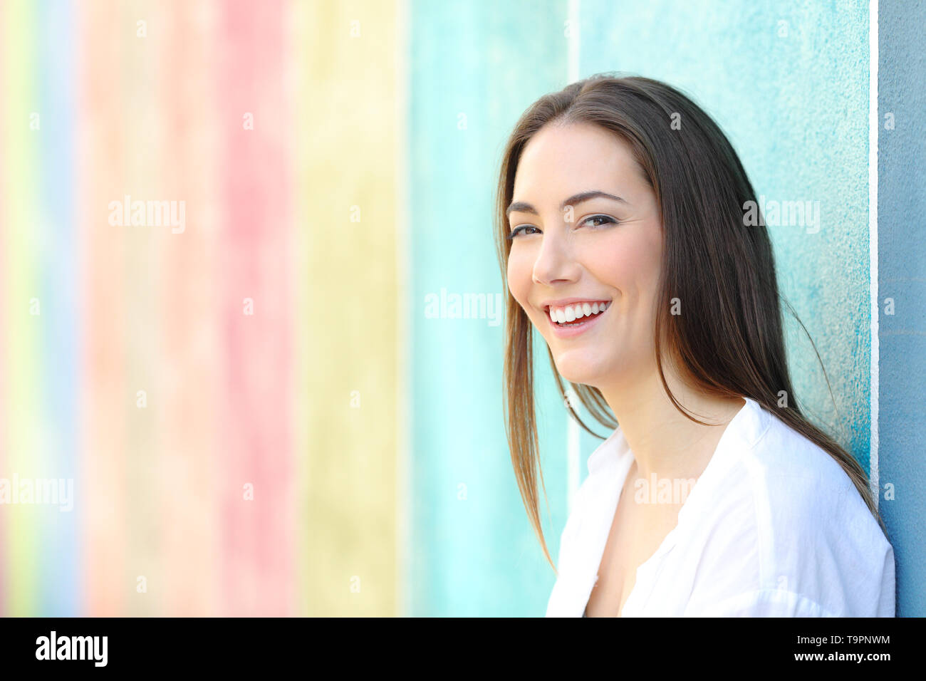 Happy woman with perfect smile looks at you leaning in a colorful wall ...