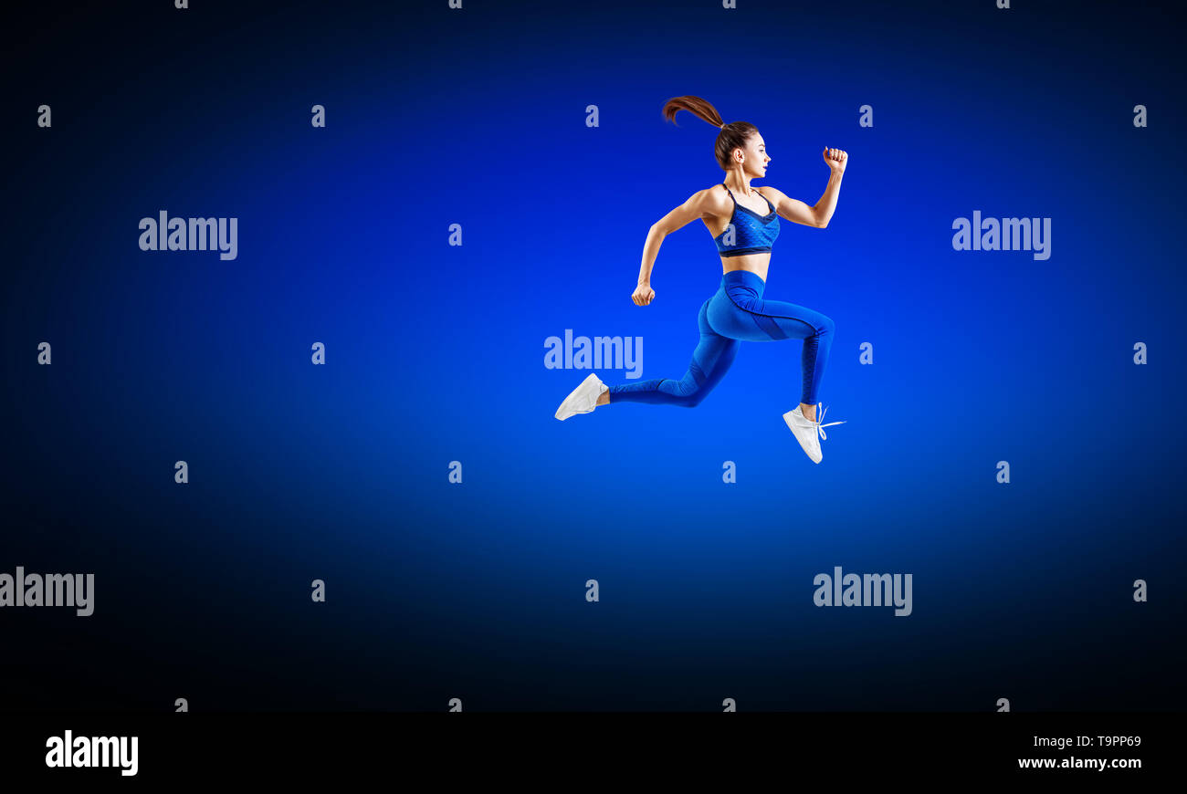 Young woman runner in blue sportswear jump in the air Stock Photo - Alamy
