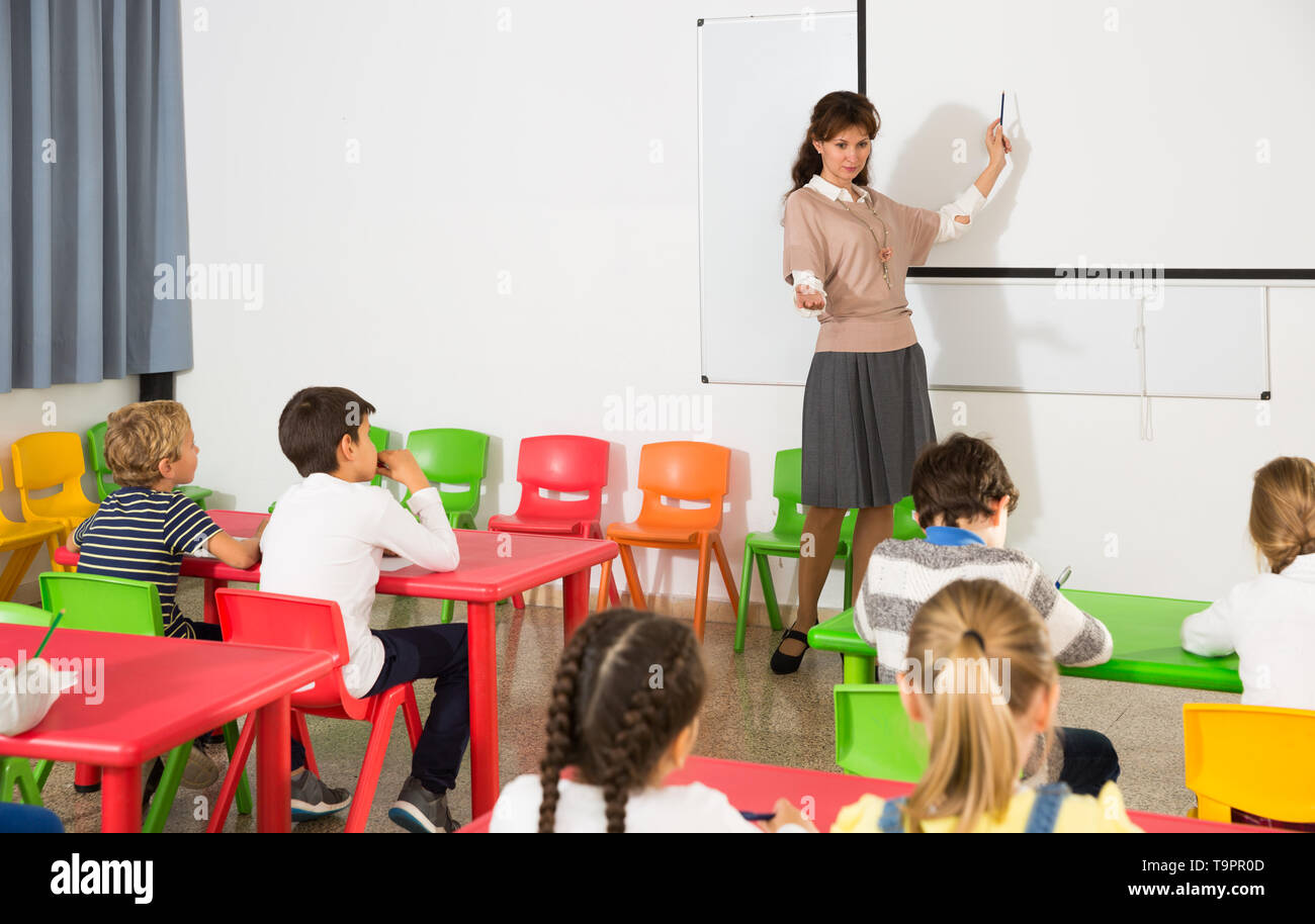 Young female teacher standing at whiteboard in classroom, conducting ...