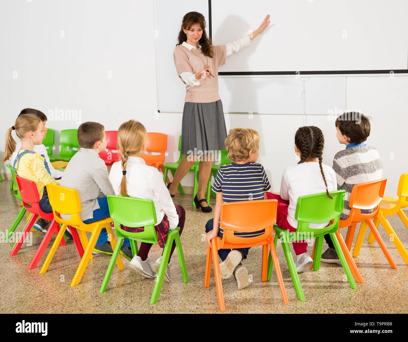 Friendly smiling teacher explaining studying material to children ...