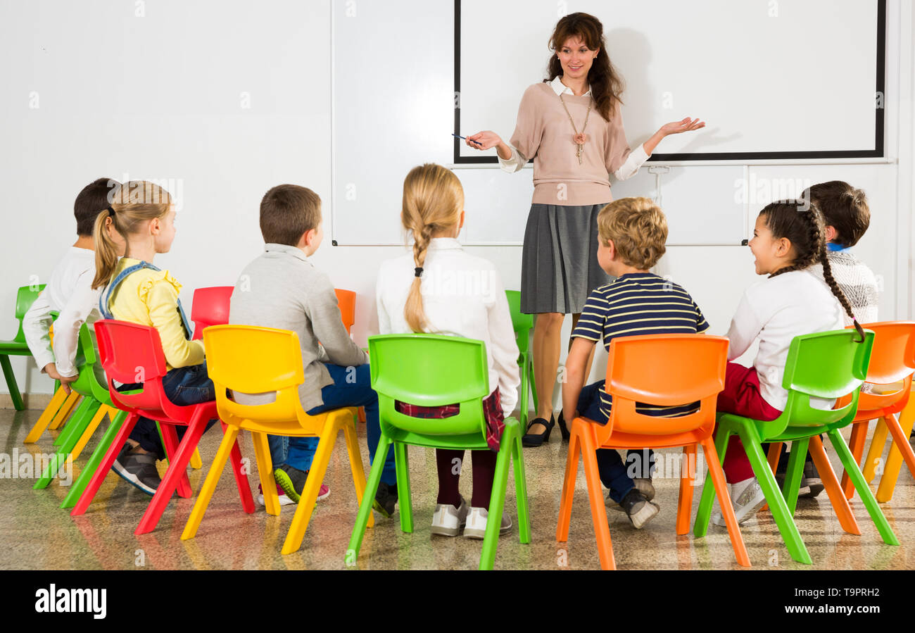 Friendly smiling teacher explaining studying material to children ...