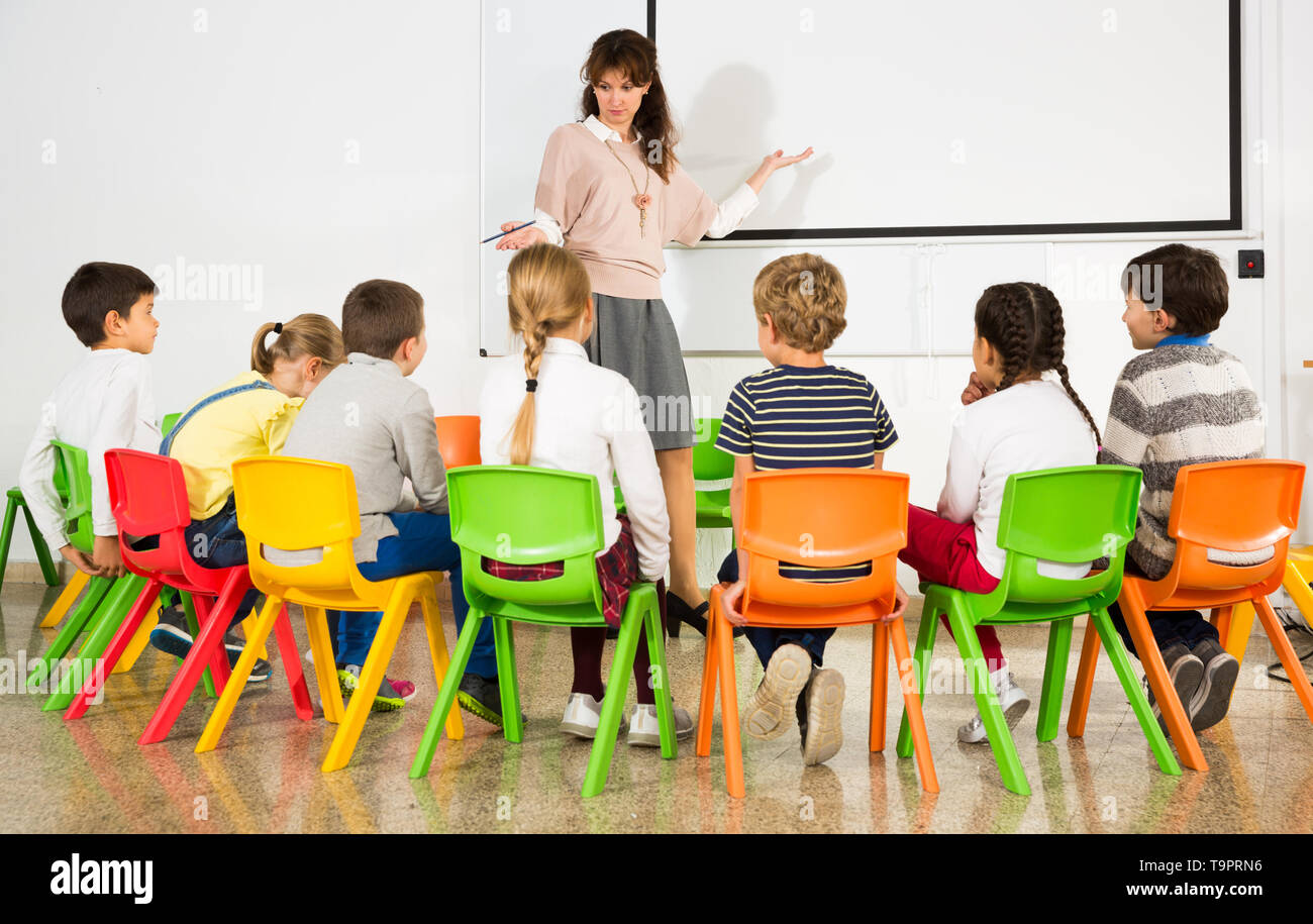 Friendly smiling teacher explaining studying material to children ...