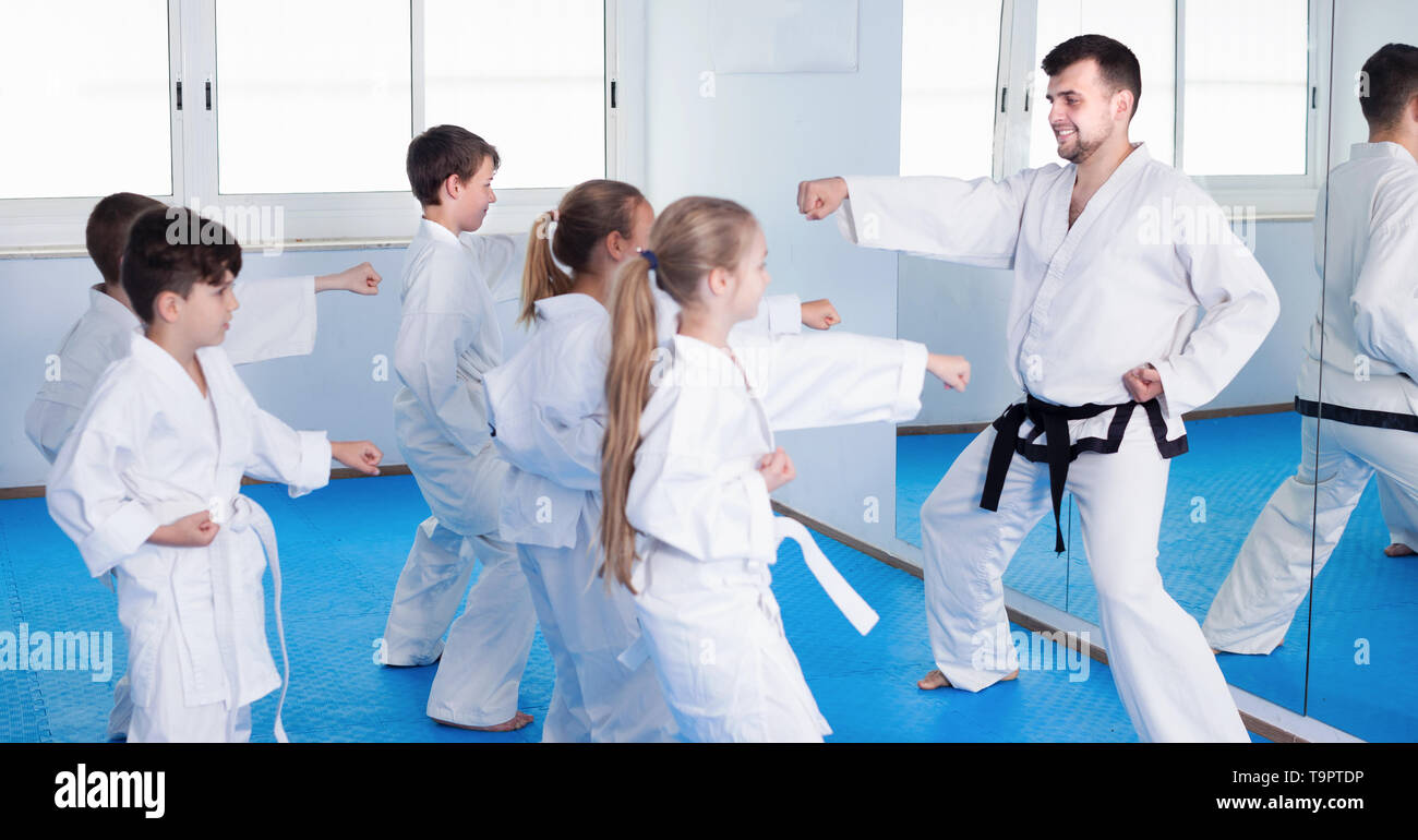 Smiling children doing karate kicks with male coach during karate class ...