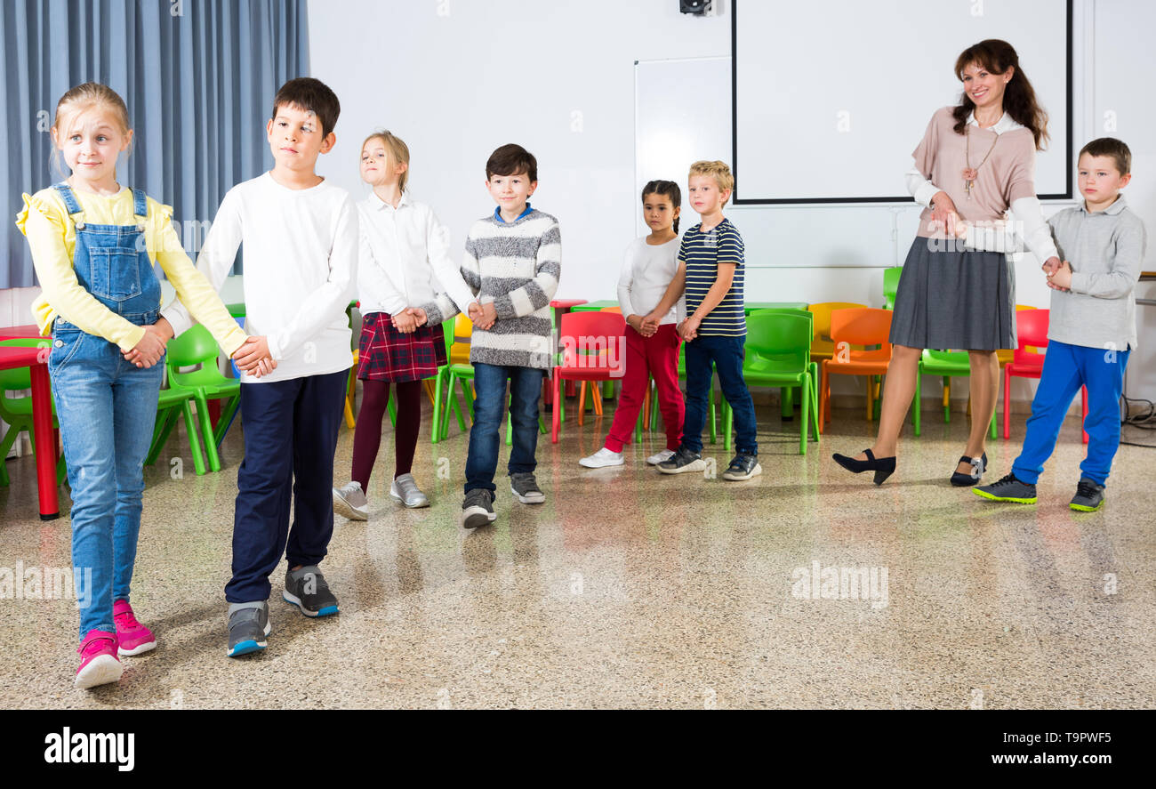 Happy kids and female teacher dancing together in classroom at ...