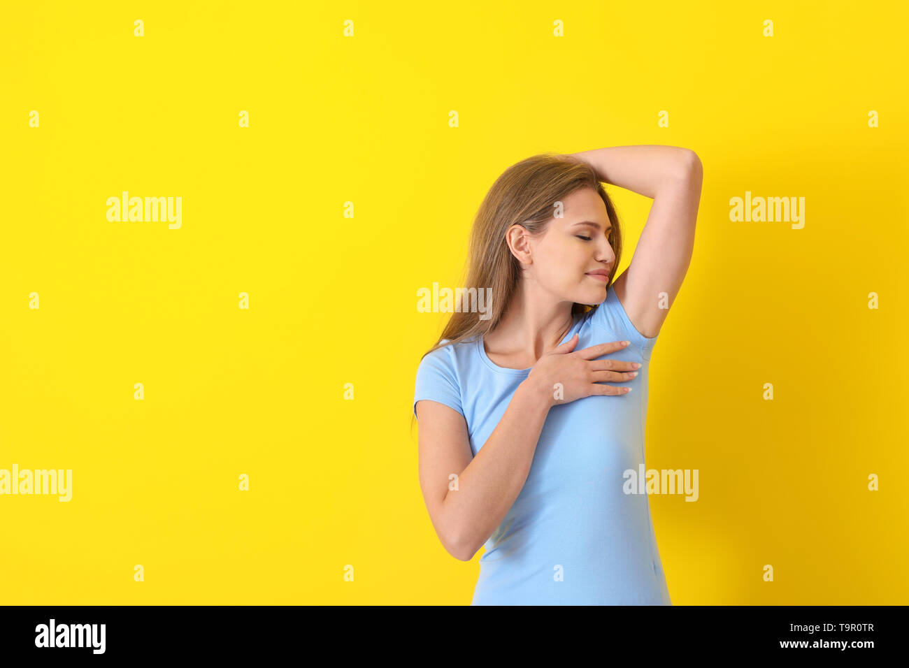 Beautiful young woman feeling smell of sweat on color background ...