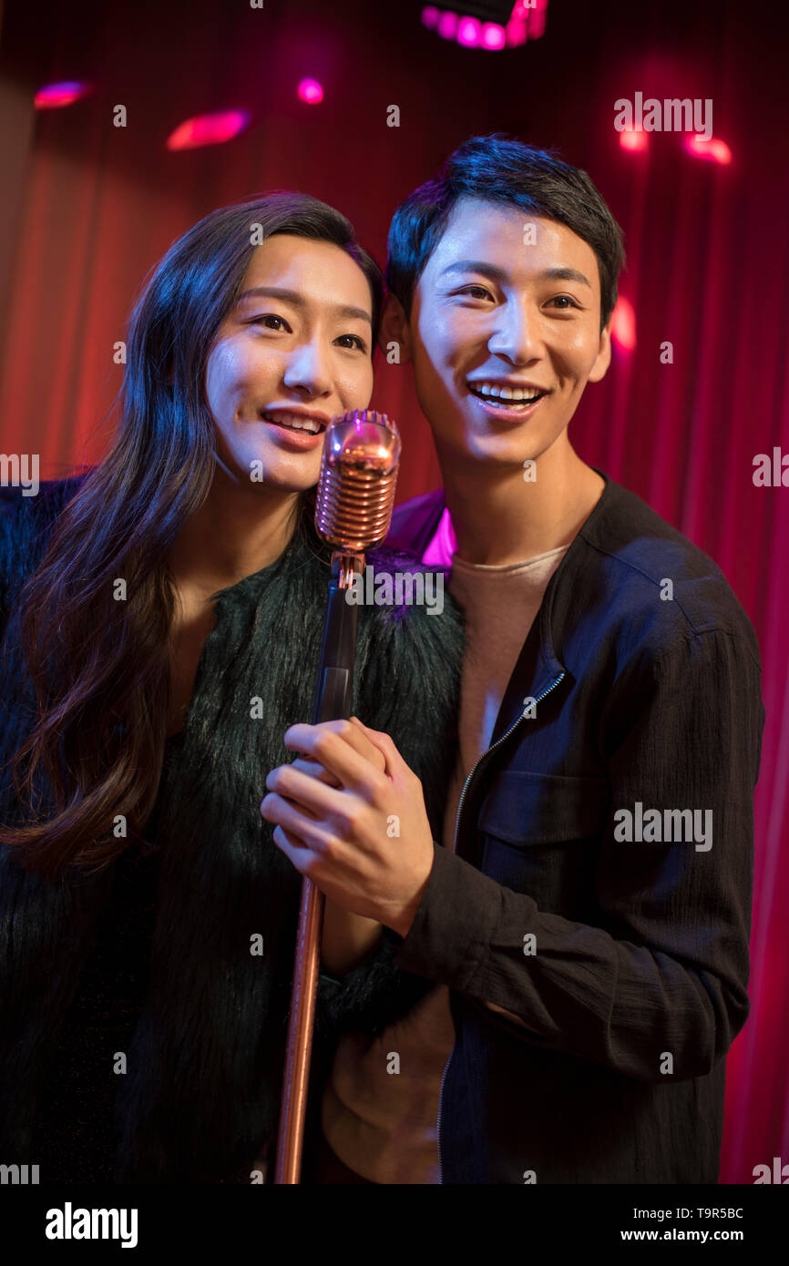 Happy young couple singing karaoke in nightclub Stock Photo - Alamy