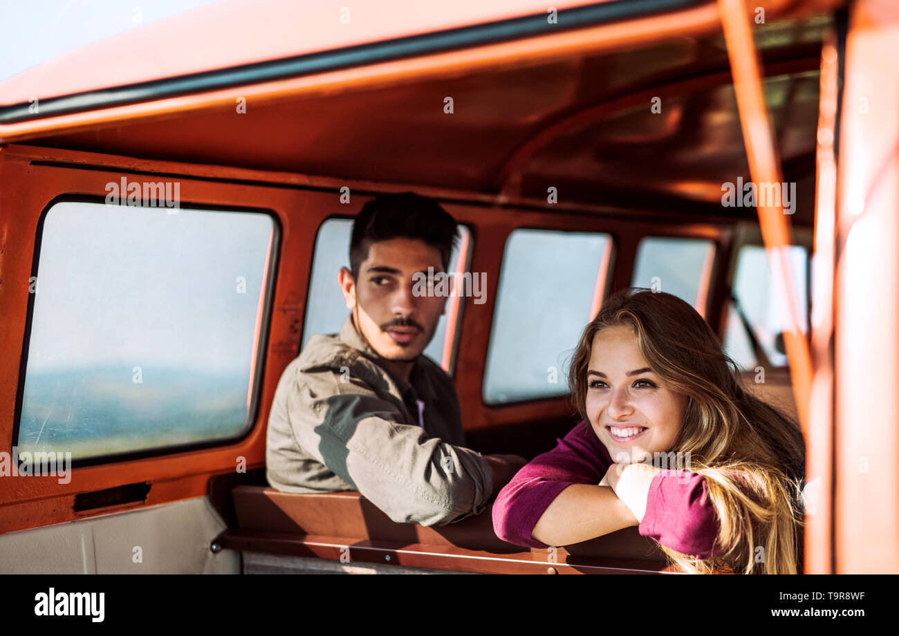 A young couple on a roadtrip through countryside, sitting in minivan ...