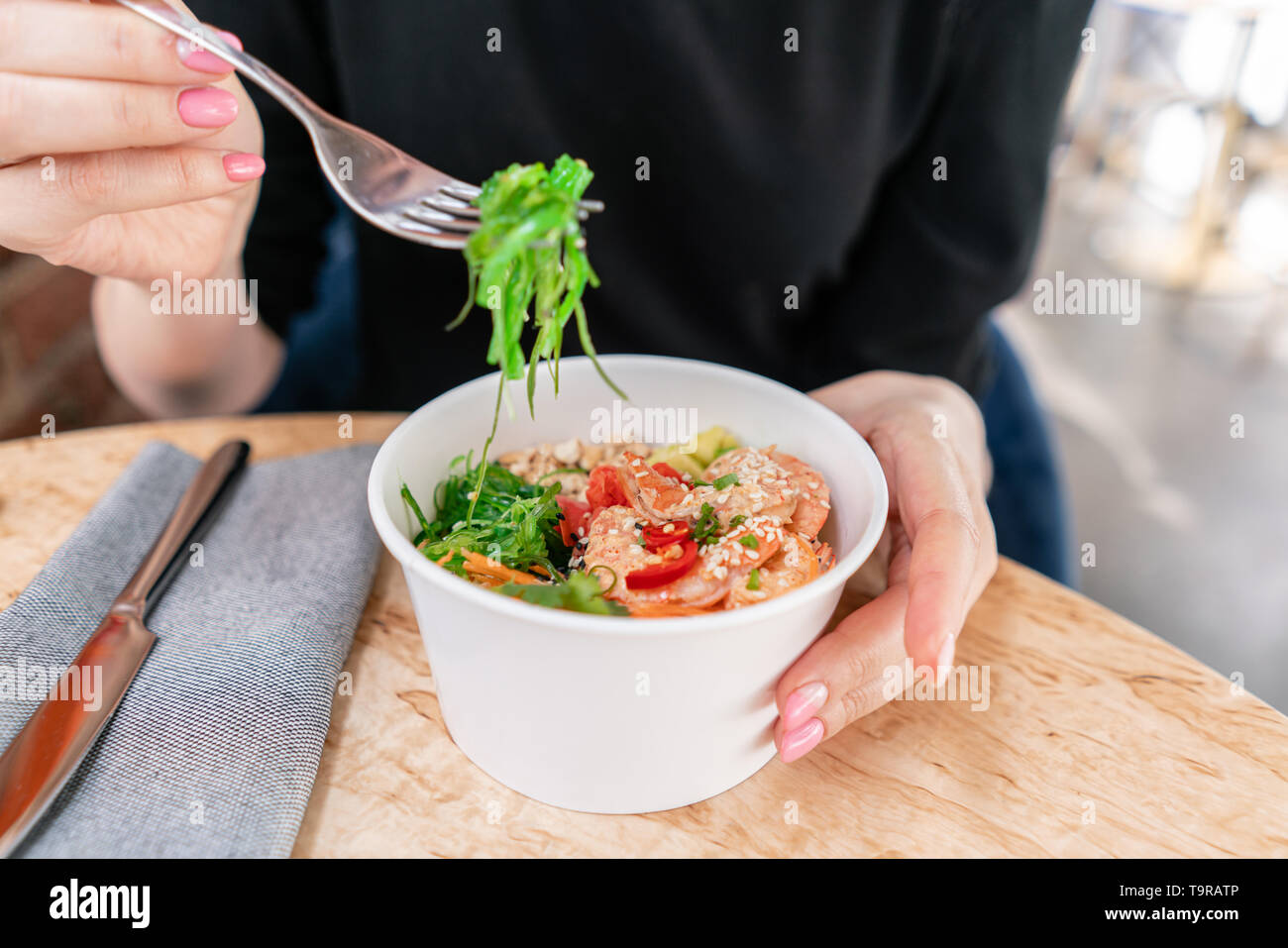 Woman eating traditional Hawaiian dish poke bowl with fork. Shrimps ...