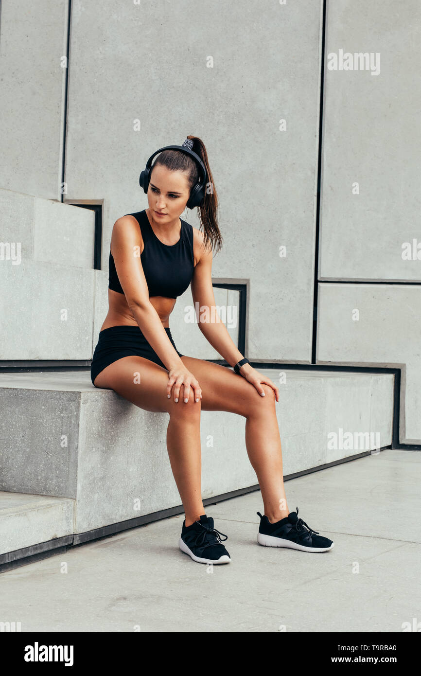 Fit young woman with headphones sitting on steps after physical ...