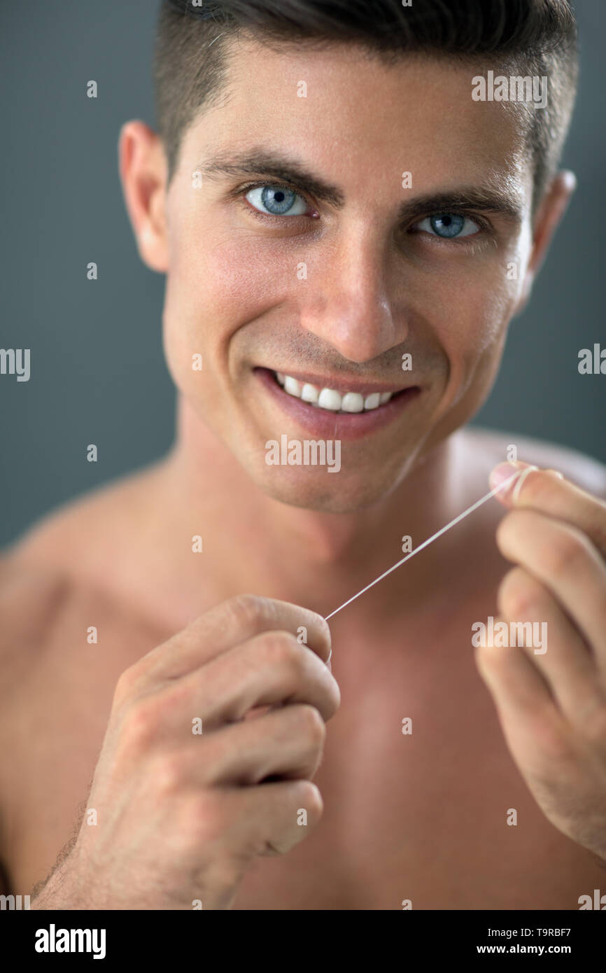 Smiling handsome young man cleaning his teeth with dental floss Stock ...