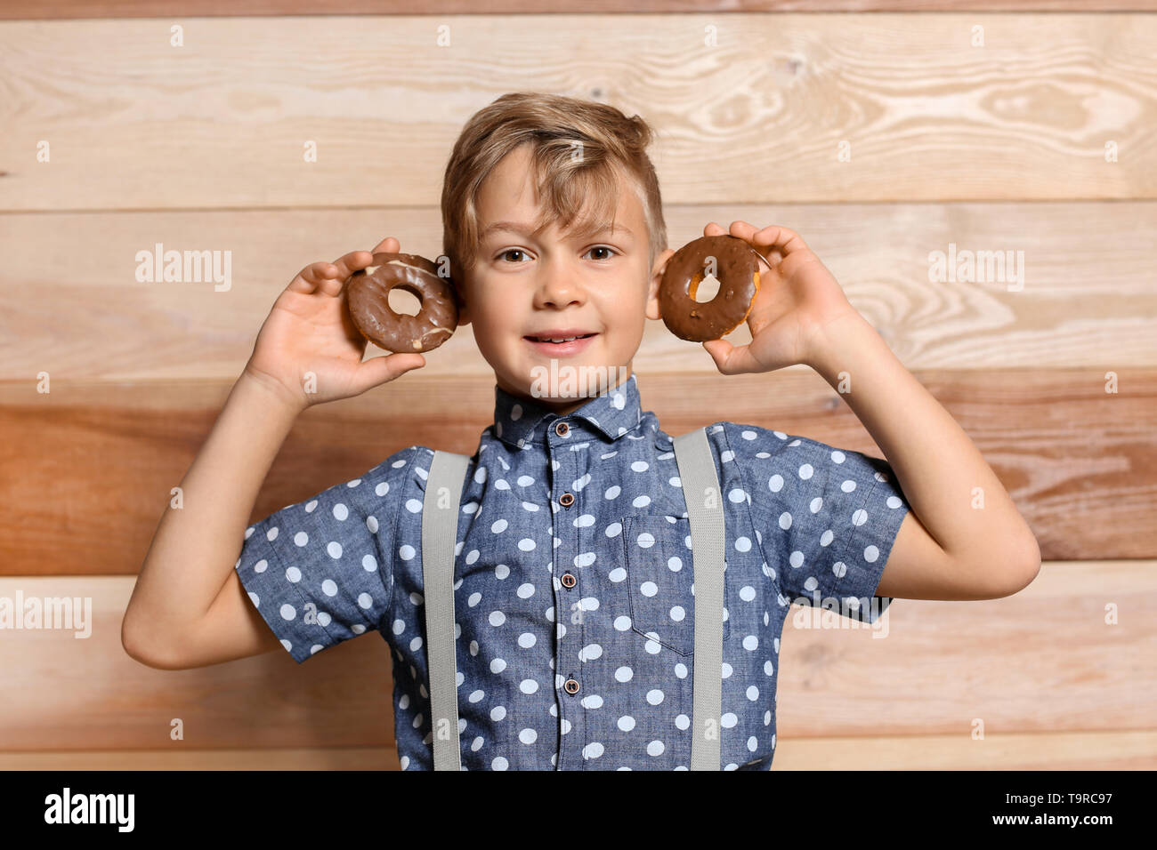 Cute little boy with donuts on wooden background Stock Photo - Alamy