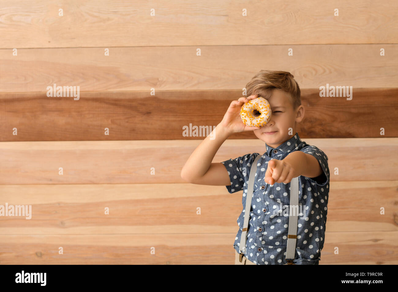 Cute little boy with donut pointing at viewer on wooden background ...