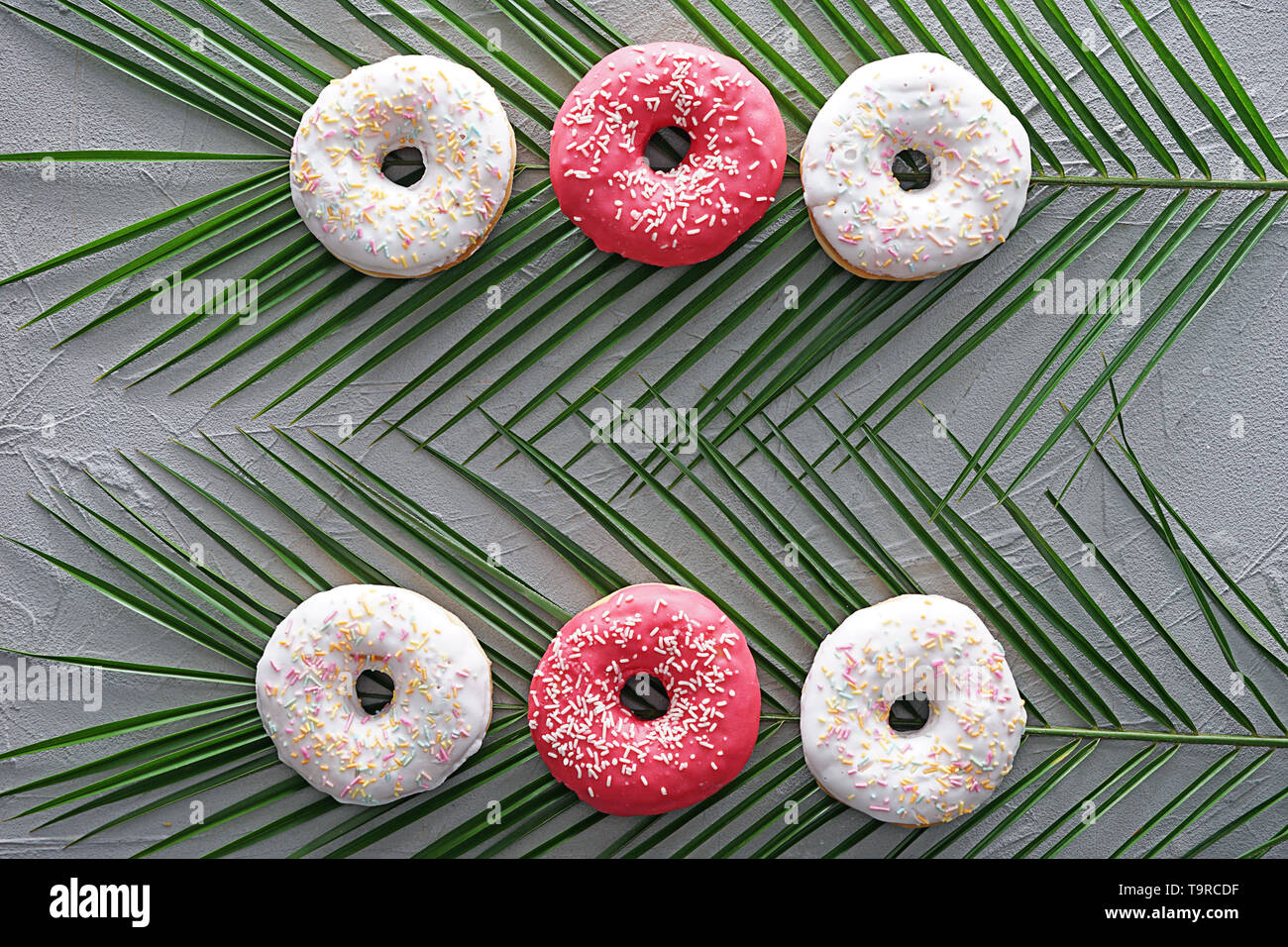 Tasty donuts and palm leaves on grey background Stock Photo - Alamy
