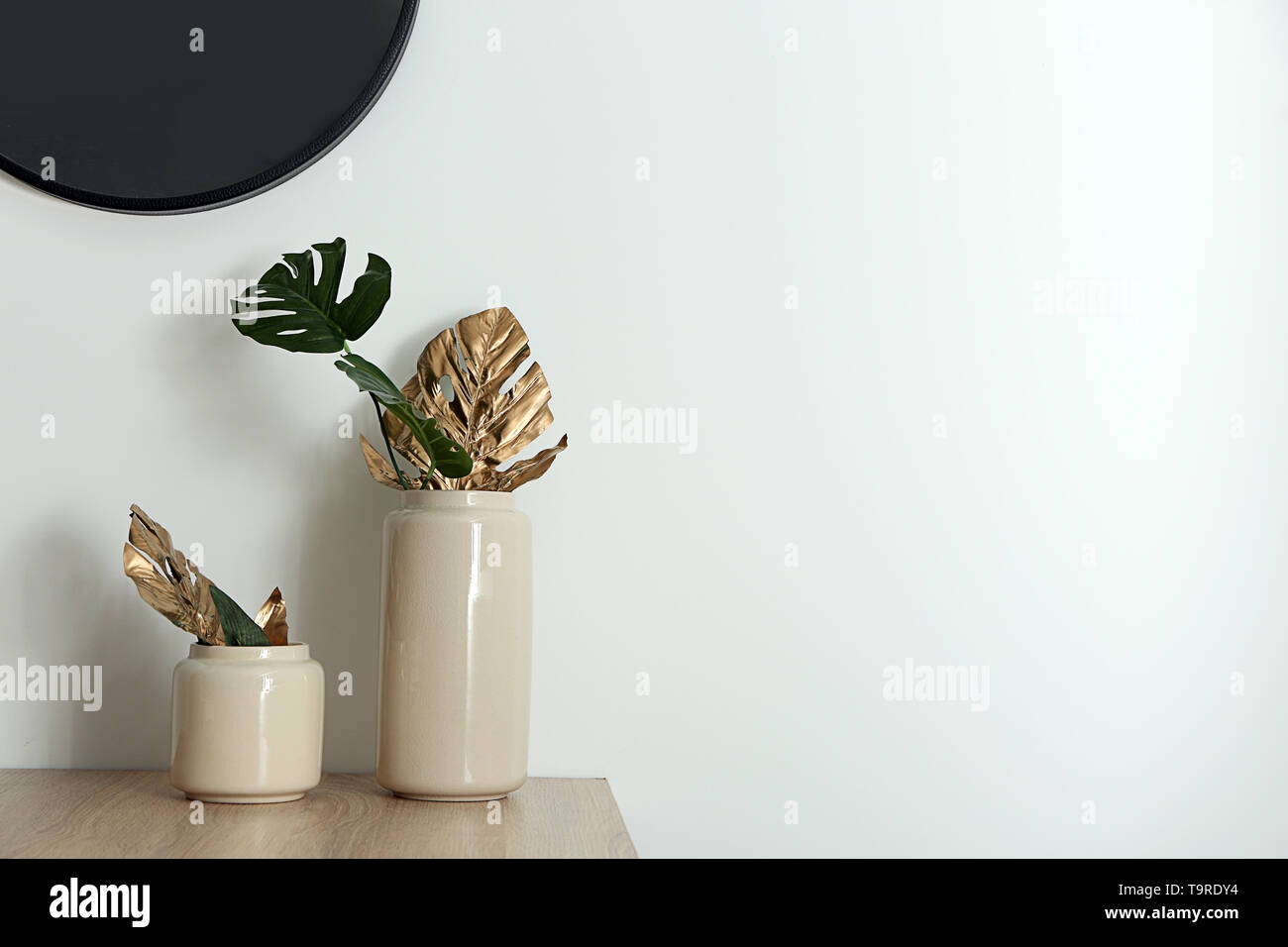 Vases with tropical leaves on table near light wall Stock Photo - Alamy