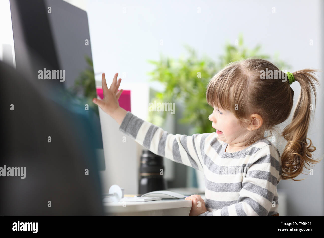 Cute little girl sitting at home at worktable working with computer ...
