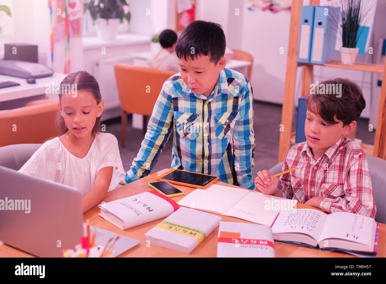 Three smiling children helping each other with homework Stock Photo - Alamy