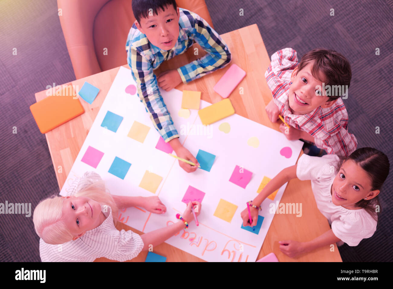 Children looking up at the camera while drawing Stock Photo - Alamy