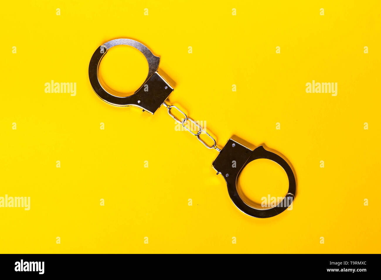 Crime concept showing handcuffs on a yellow background with copy space ...