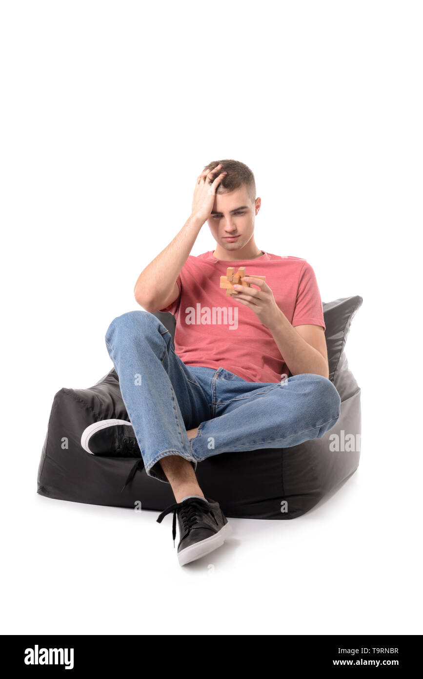 Young man with brain teaser sitting on frameless armchair against white ...