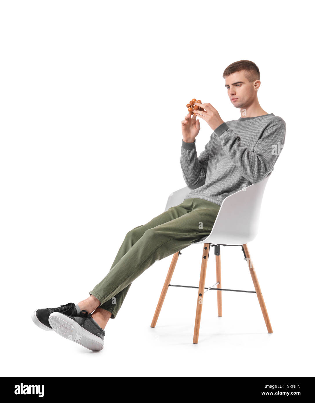 Young man with brain teaser sitting in armchair on white background ...