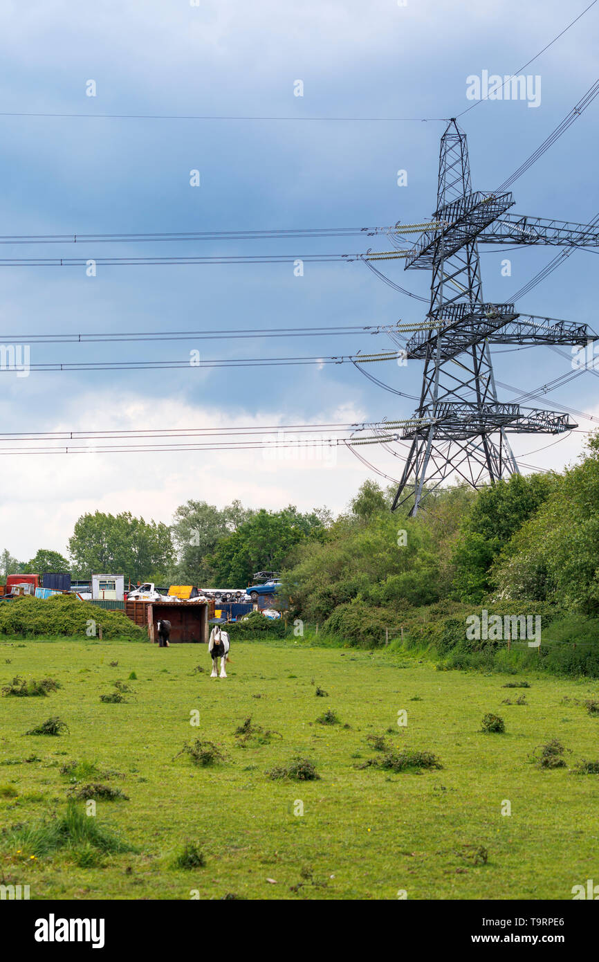 View across a field of a large electricity pylon, power lines and car ...