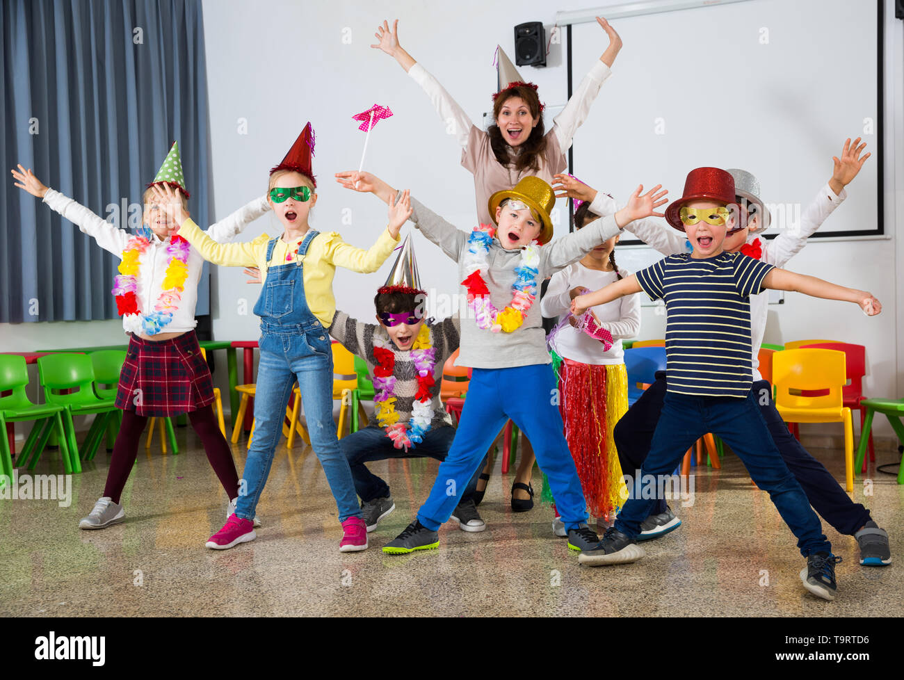 Cheerful pupils and female teacher with funny hats and festive ...