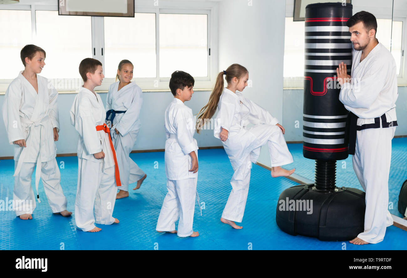 Diligent children training karate kicks on punching bag during karate ...