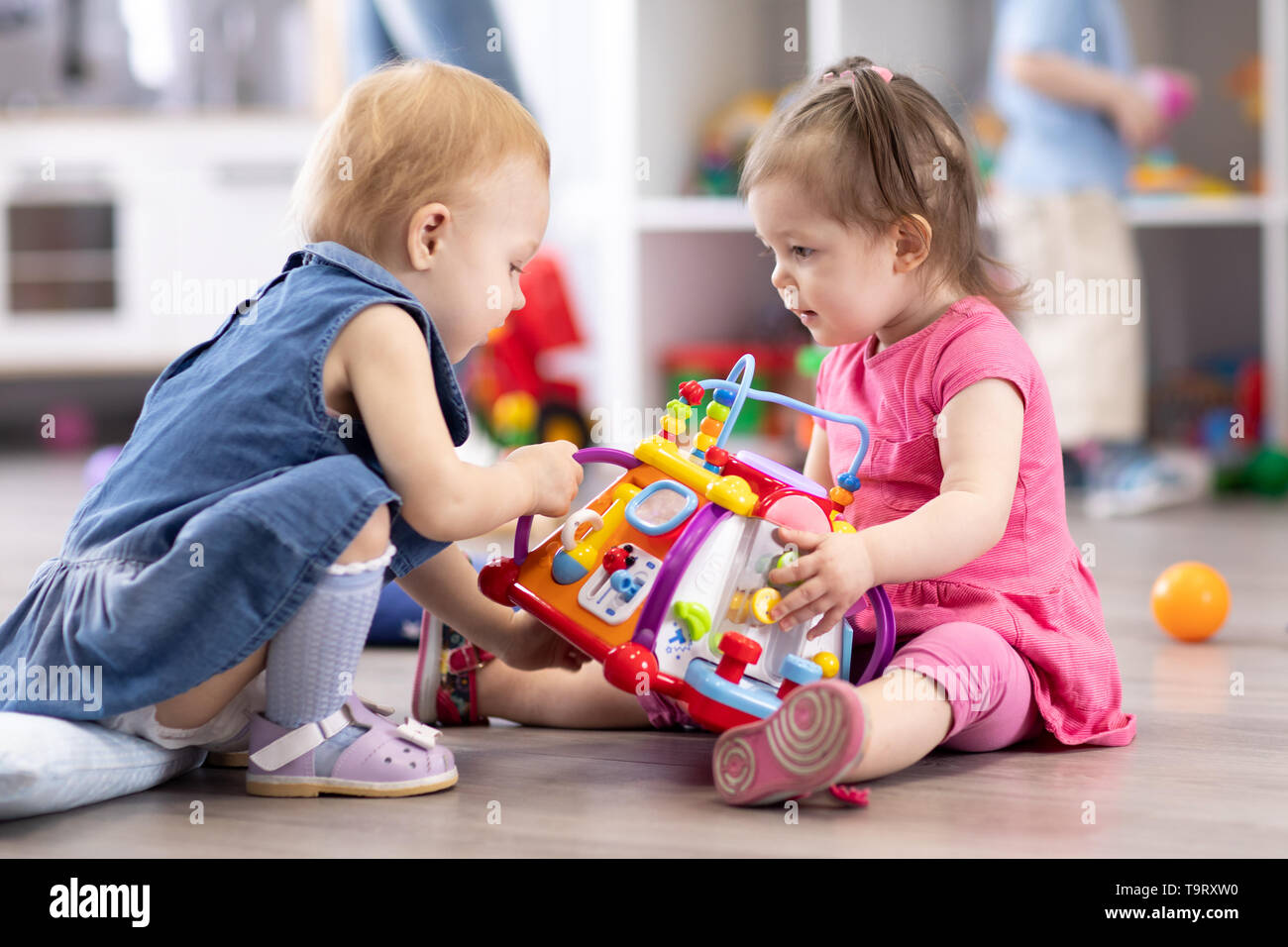 Babies conflict in nursery. Child girl trying to take away toy from ...