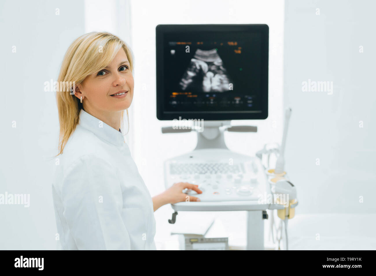 Portrait of smiling Gynecologist sitting by ultrasound machine at her ...
