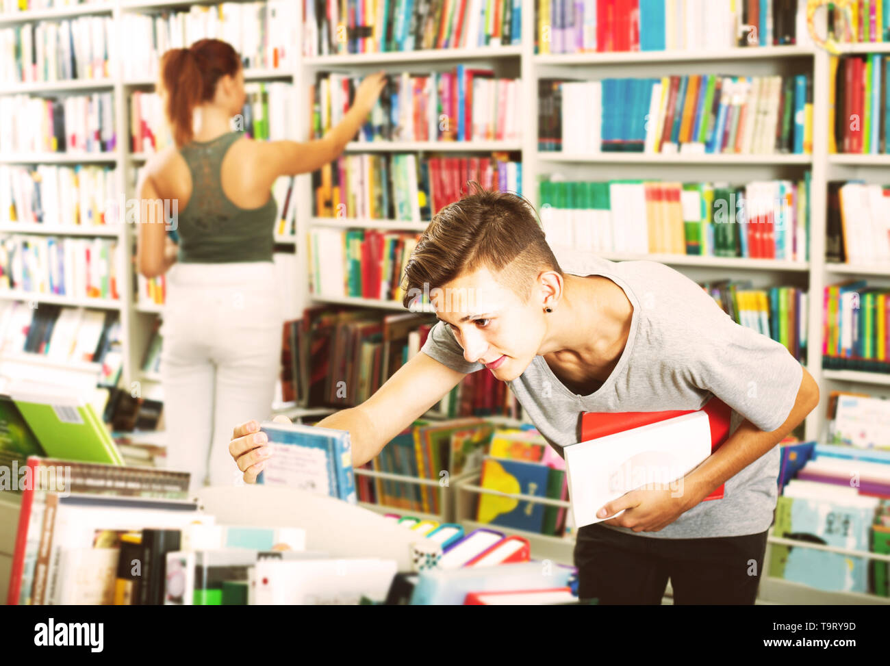 Positive teenager boy searching for new book on shelves in store Stock ...