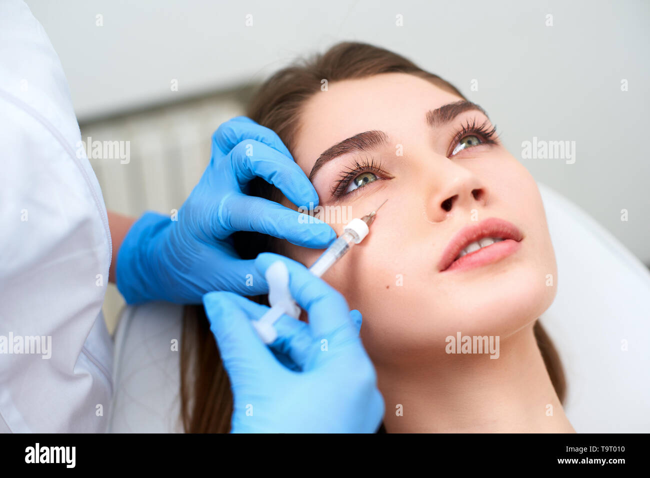 Doctor in medical gloves with syringe injects botulinum under eyes for ...
