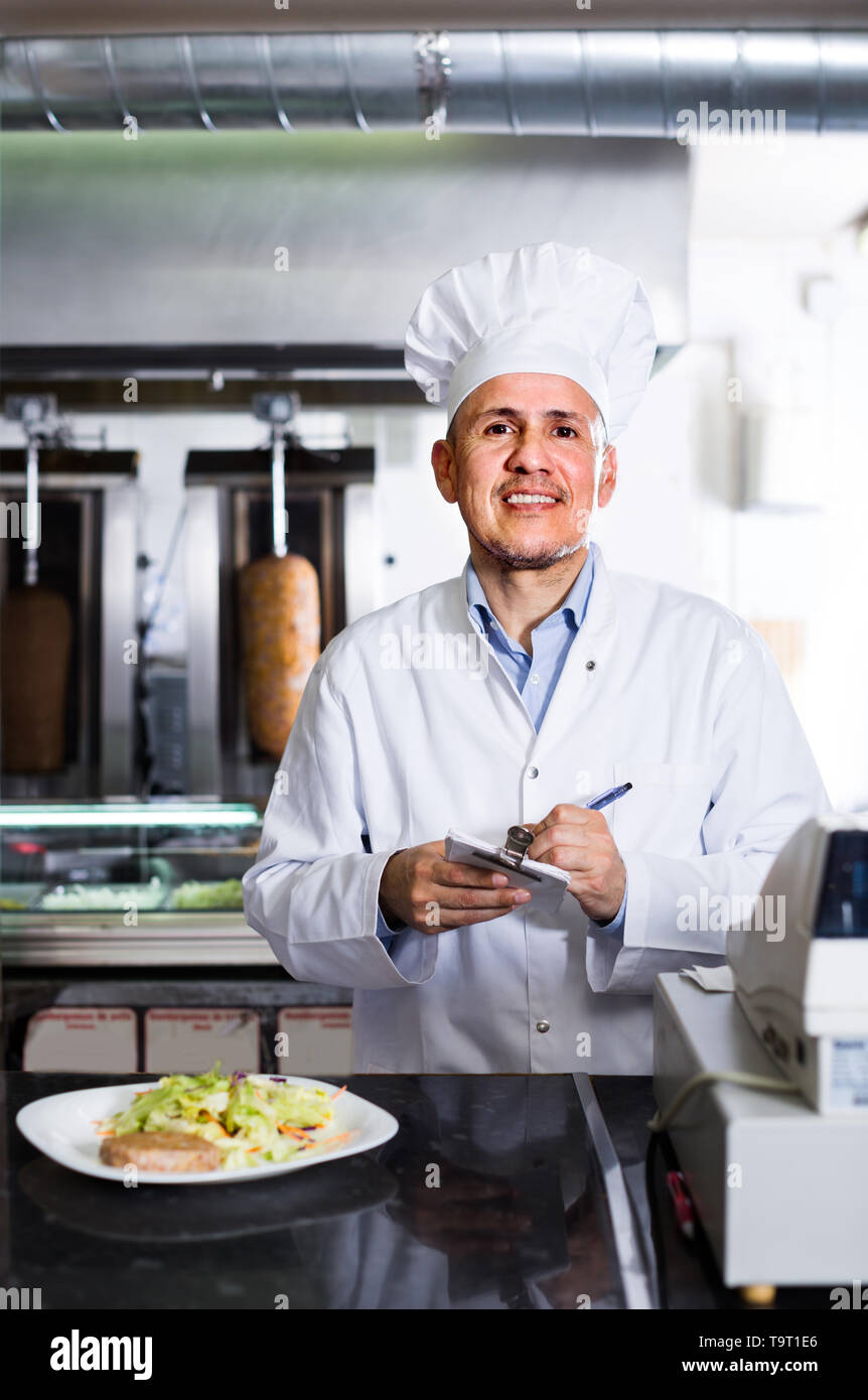 smiling mature man chef in uniform taking order from customer in fast ...