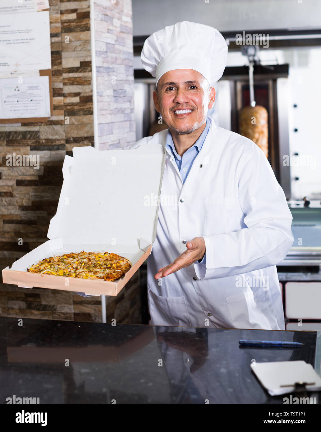 Mature man cook wearing uniform serving fresh pizza to customer in fast ...