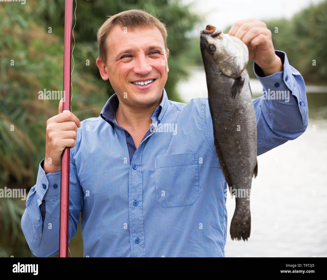 Smiling fisherman holding catch freshwater fish in hands on lake Stock ...