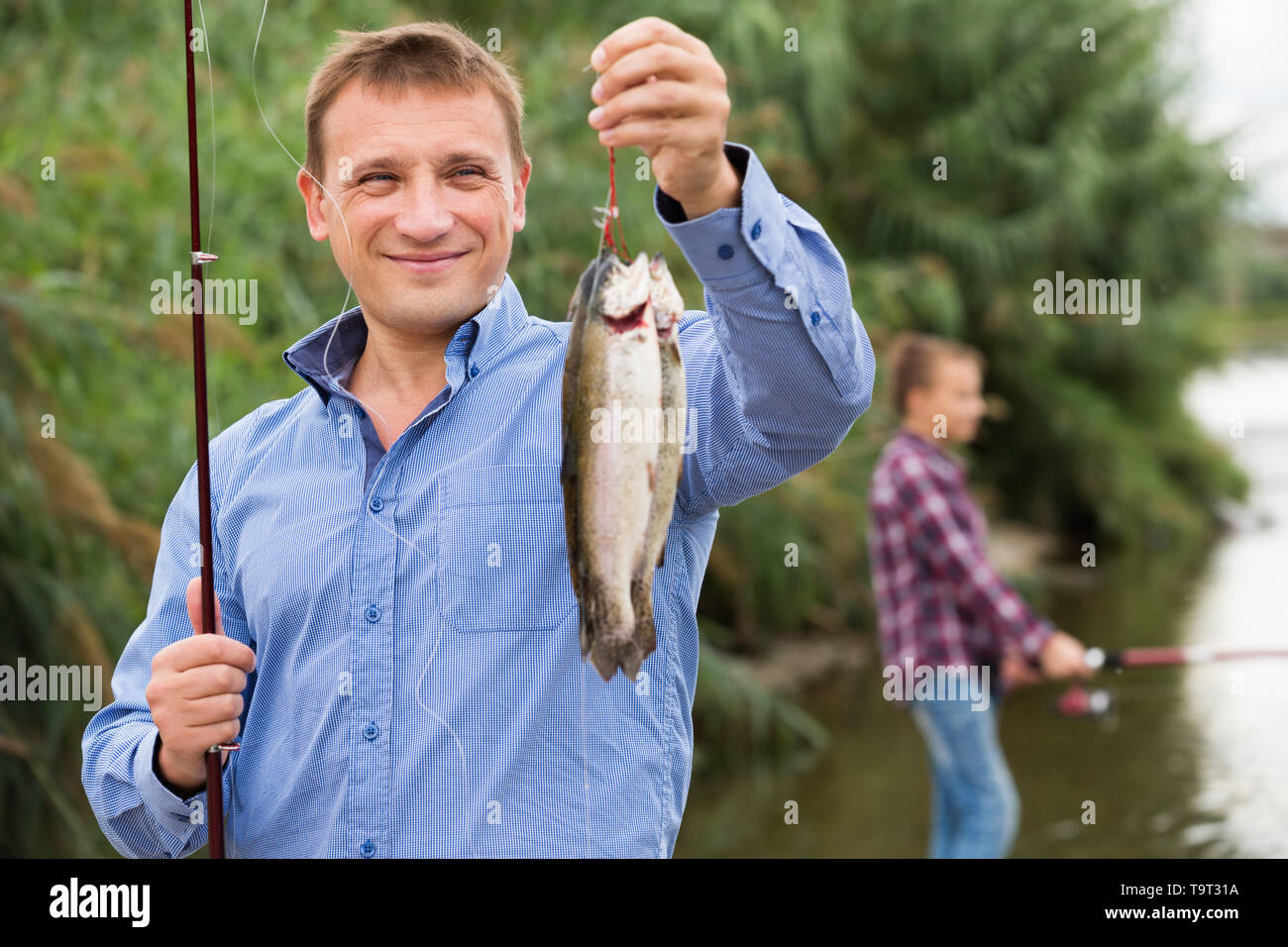 Glad man holding a fish after fishing on the river side Stock Photo - Alamy
