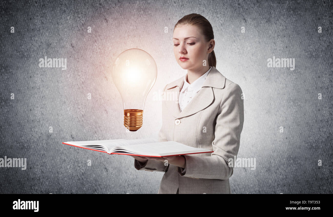 Woman showing shining light bulb on open book Stock Photo - Alamy