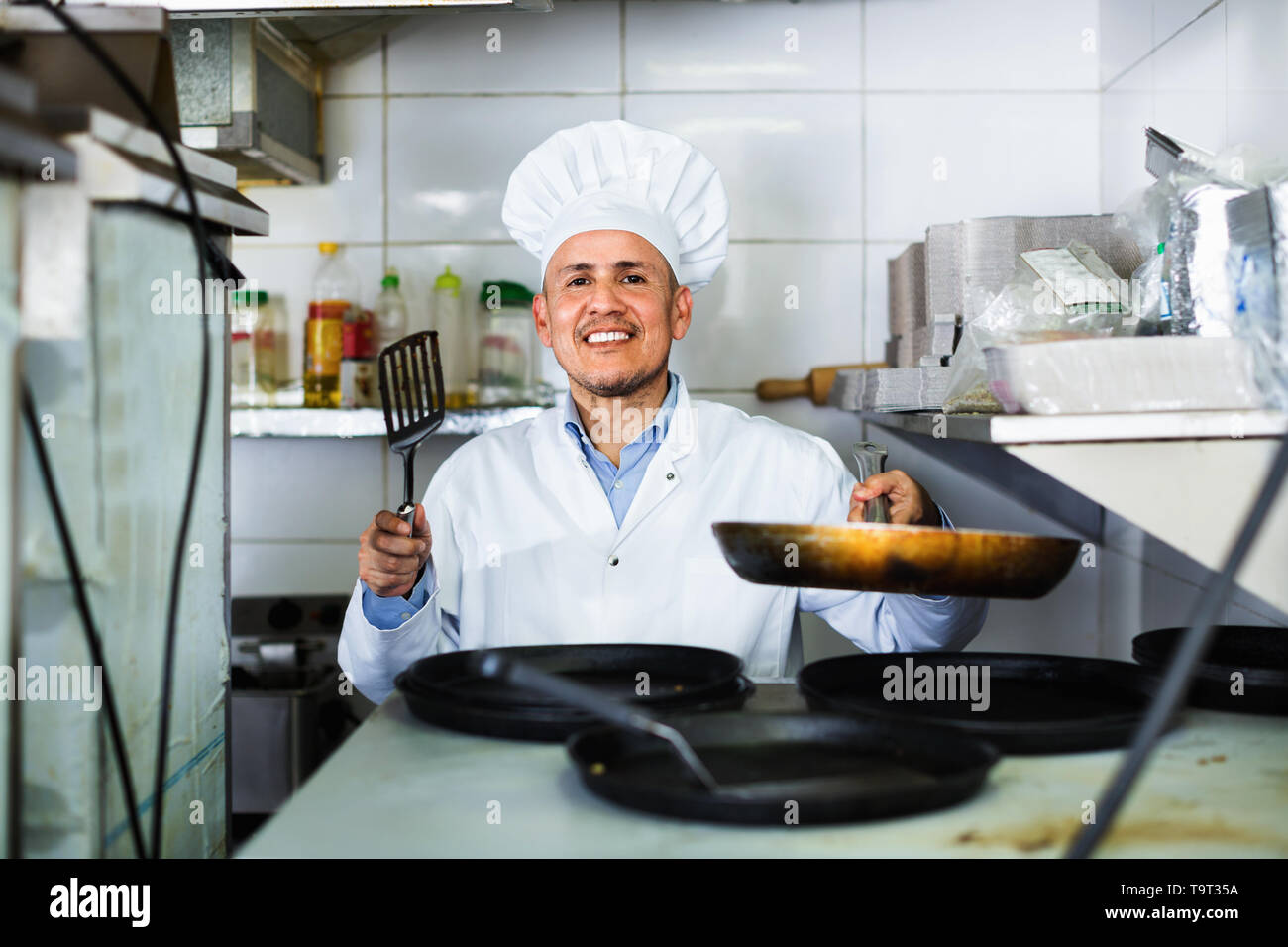 Portrait of cheerful smiling mature man cook with frying pans on ...