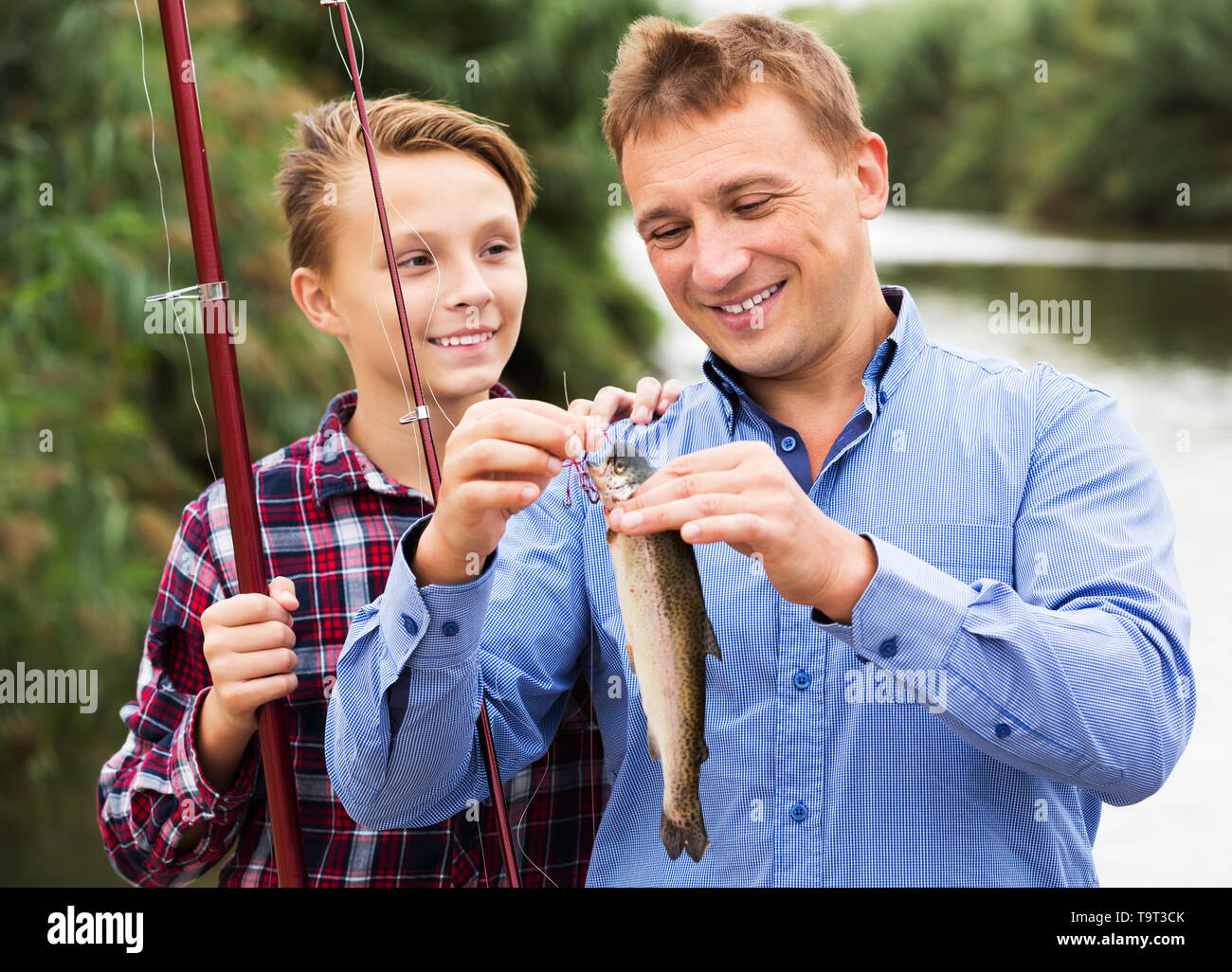 Portrait of smiling teenage boy and his father holding taken freshwater ...