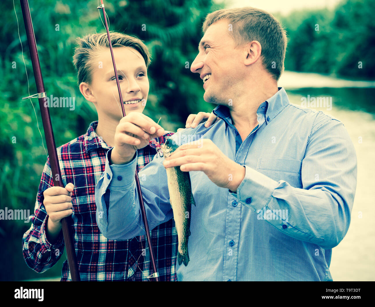 Handsome man with teenager boy releasing fish from hook outdoors. Focus ...