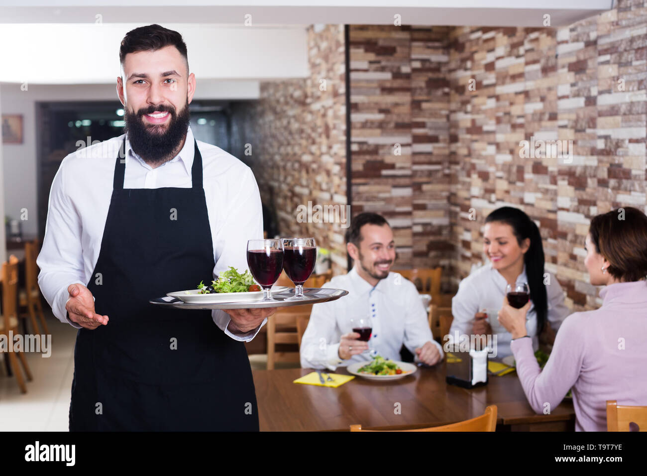 Positive male waiter welcoming guests to country restaurant Stock Photo ...