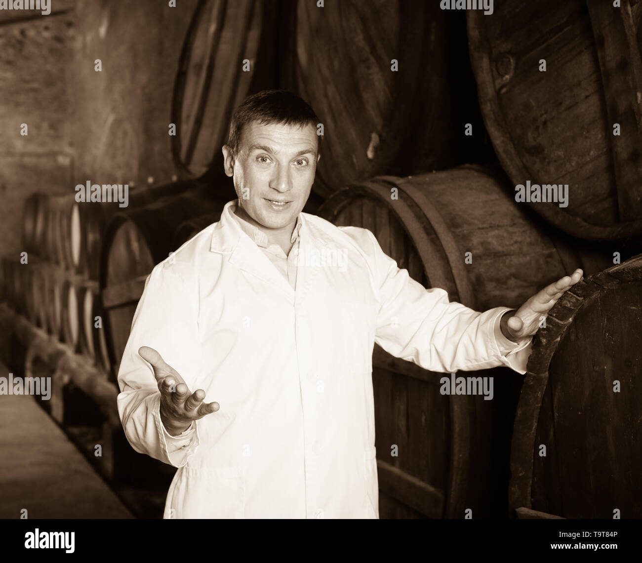 Adult worker of winery posing with wine barrels in cellar Stock Photo ...