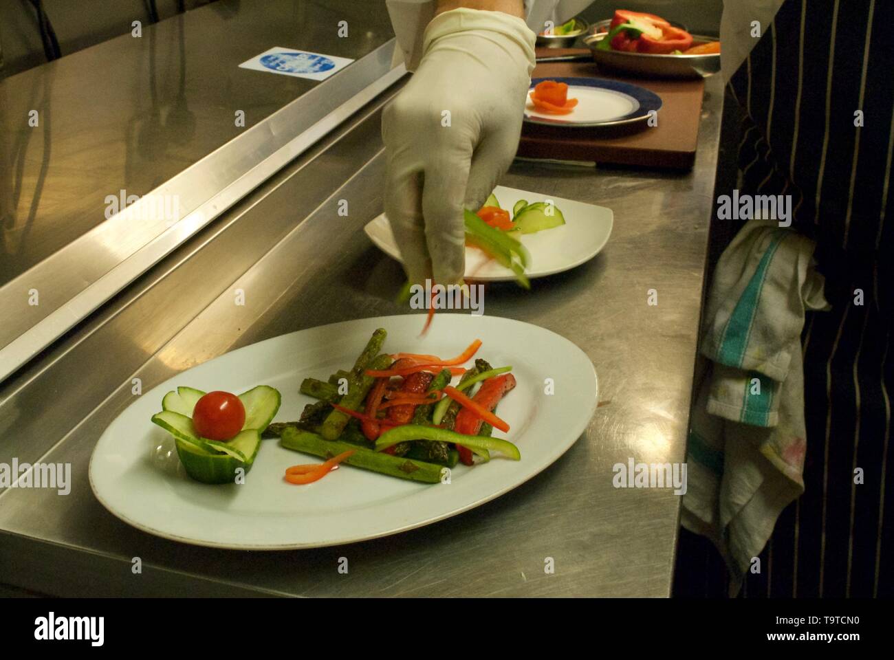 A professional chef preparing a salad garnish in a restaurant kitchen ...
