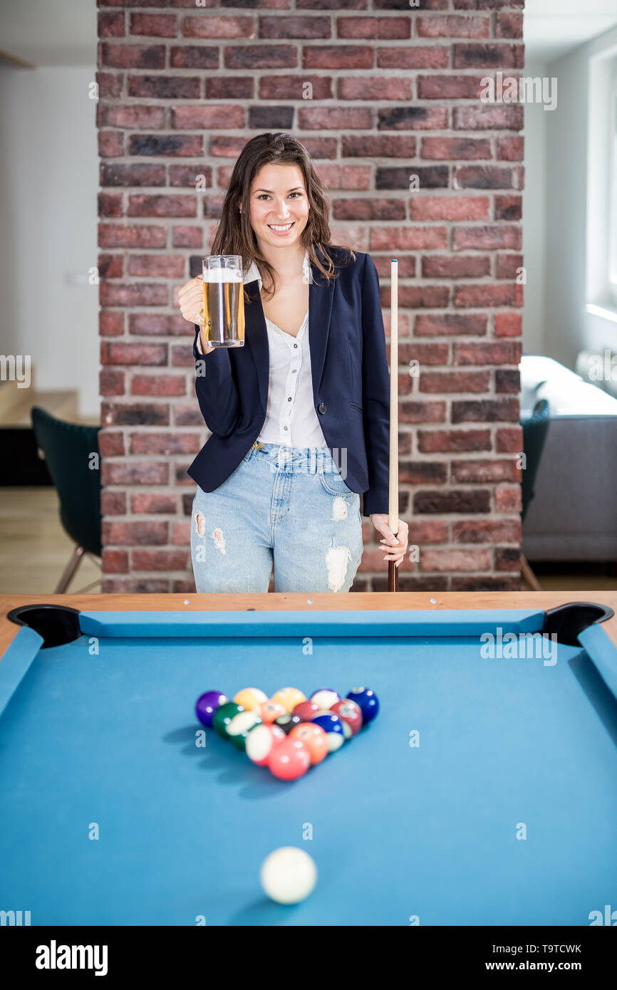 Beautiful female billiard player holding beer mug next to pool table ...