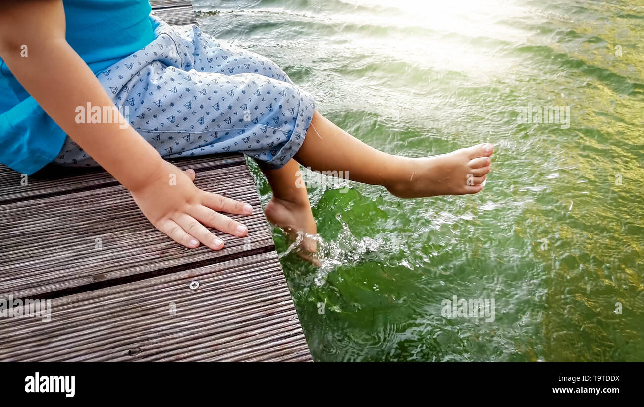 Closeup photo of 3 years old little boy sitting on the wooden pier and ...