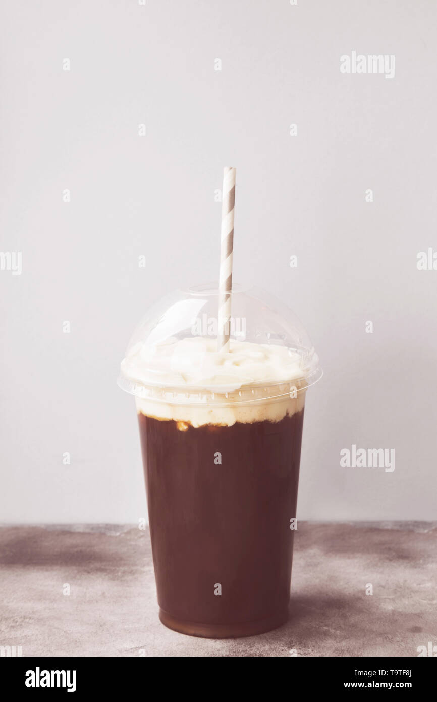 Coffee in plastic takeaway cup with cream on gray background. Toned ...