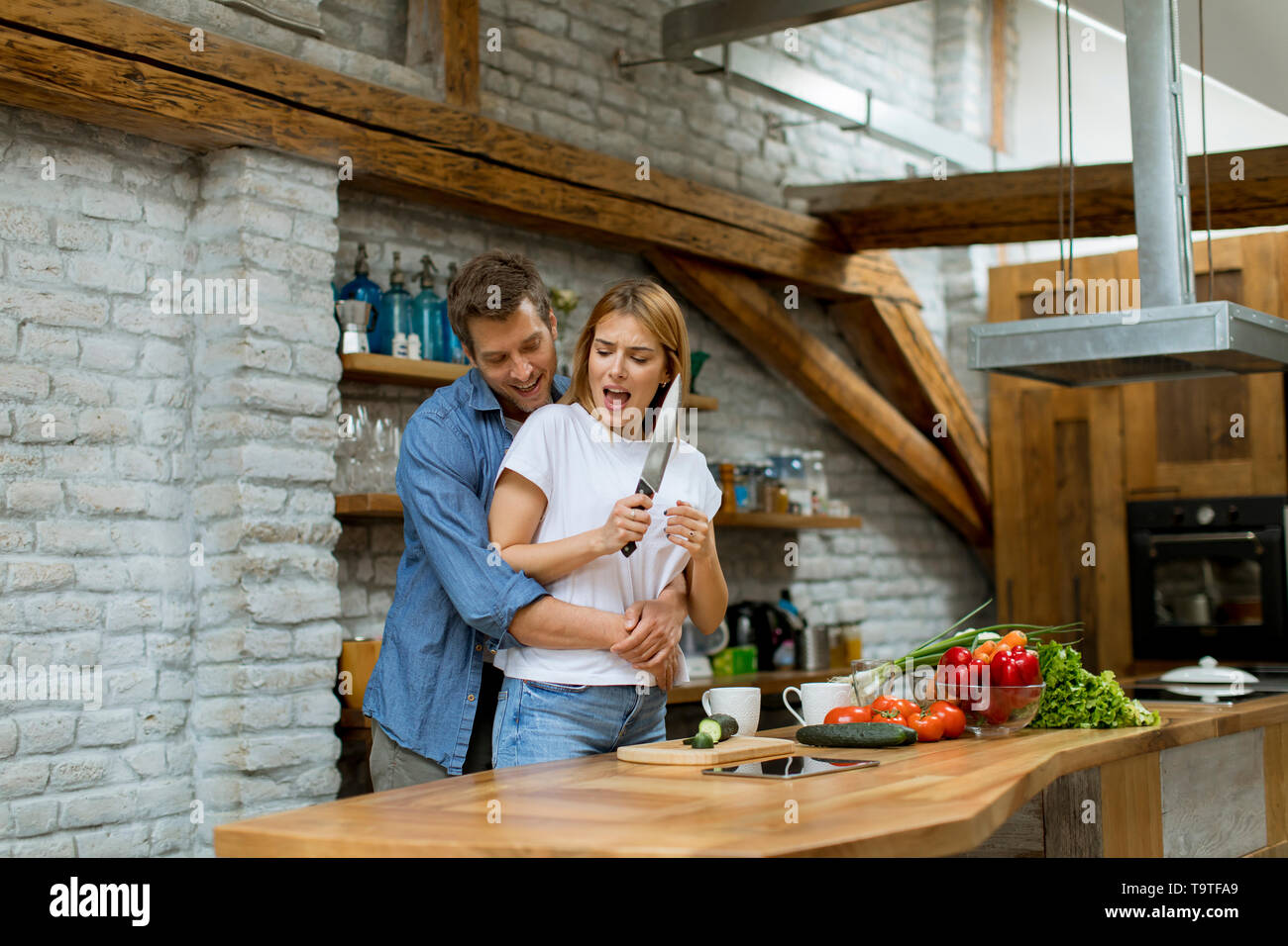 Lovely cheerful young couple cooking dinner together and having fun at ...