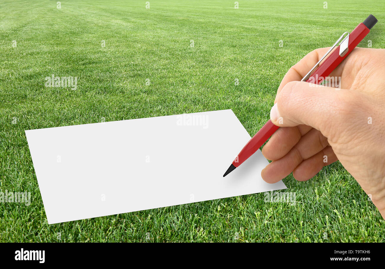 Hand writing with a pencil on a blank sheet over a beautiful green ...