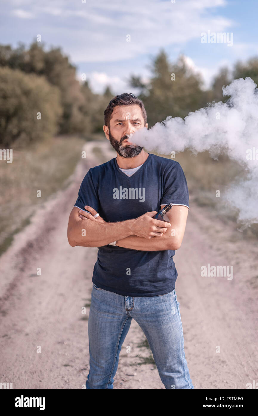 Modern smoker vaping an electronic cigarette in the woods. Smoking ...