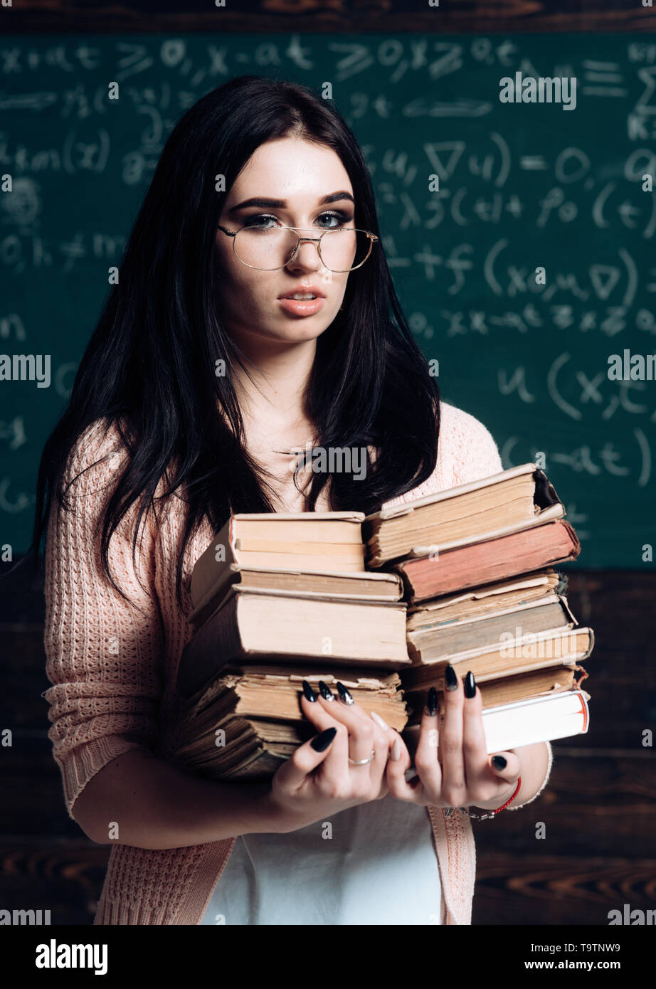 Lovely female student with heap of books standing in classroom ...